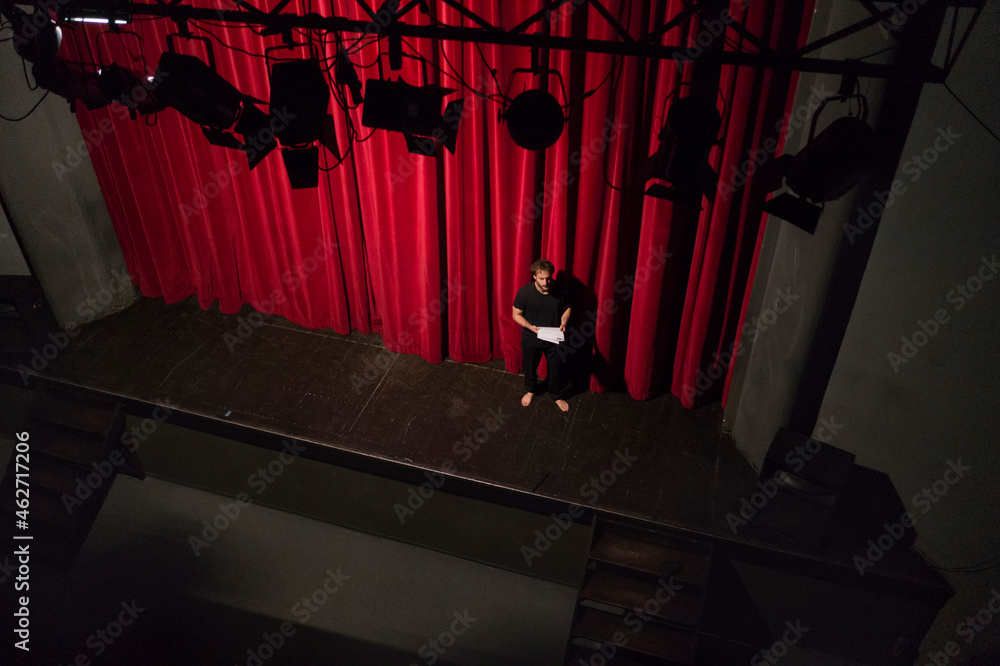 Barefoot actor with script standing on theatre stage in front of red ...