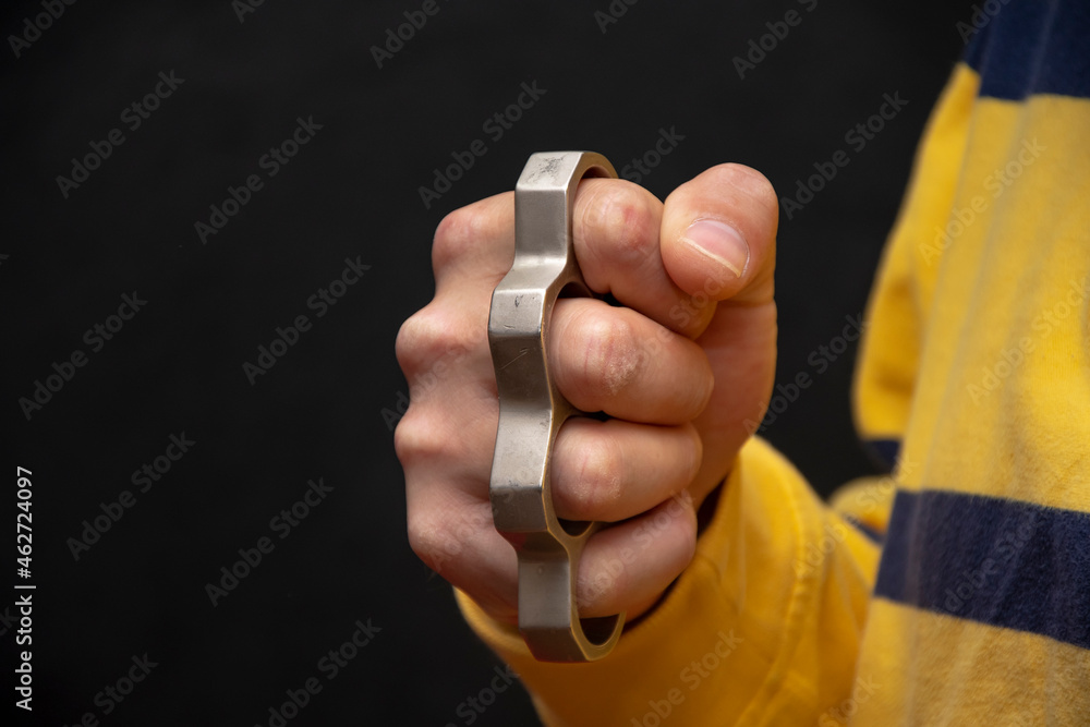 Male hand squeezes metal brass knuckles on a black background. Concept ...
