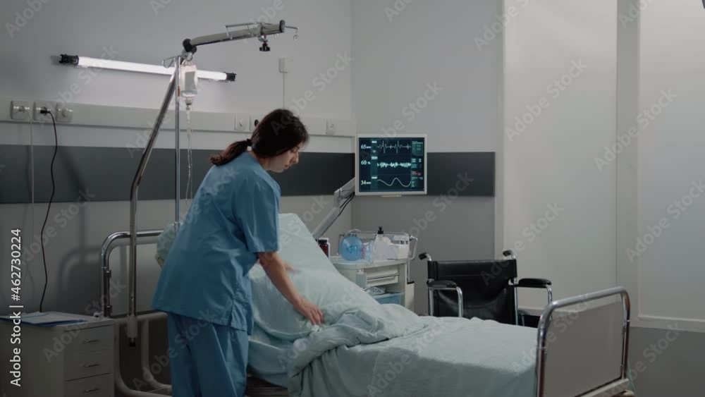 Medical assistant preparing hospital ward bed for patient at facility ...