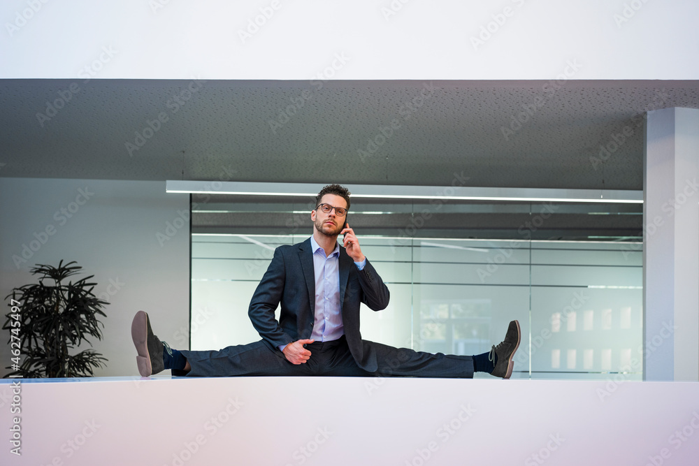 Businessman doing the splits on reception desk in office talking on ...