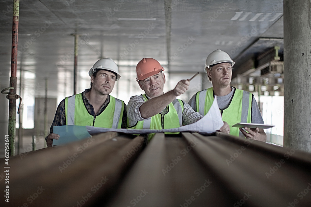 Male construction worker discussing plan with coworkers at construction ...