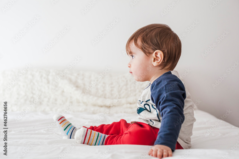 Side view of baby boy sitting on bed looking at distance Stock Photo ...