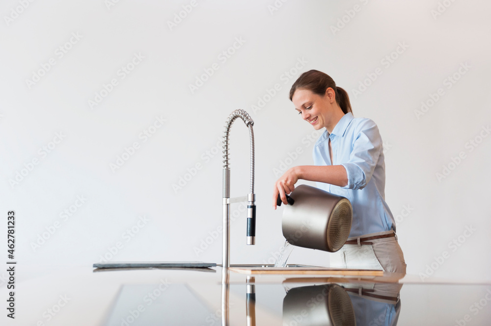 Smiling mid adult woman pouring water in modern kitchen sink while ...