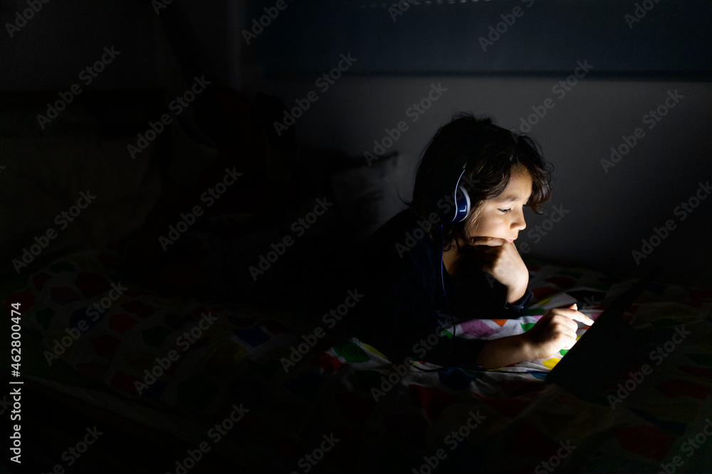 Boy lying on bed at home using headphones and digital tablet Stock ...