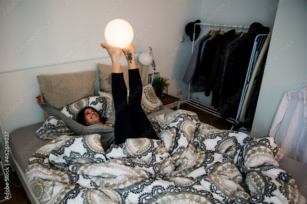 Woman lying on bed, balancing ball-shaped lamp on her feet Stock Photo ...