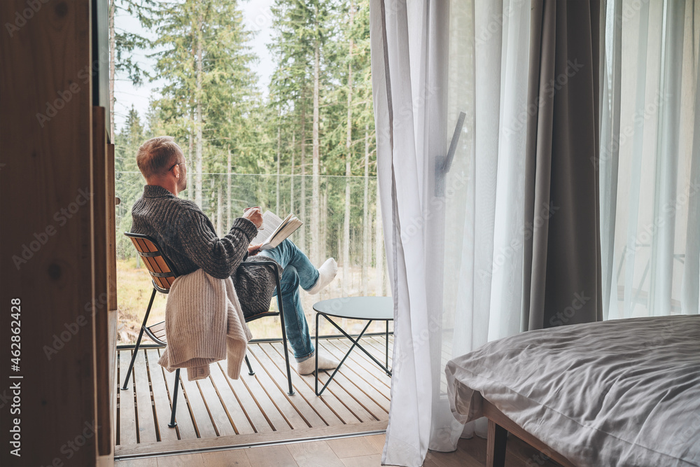 Alone man sitting in chair on country house balcony and enjoying forest ...