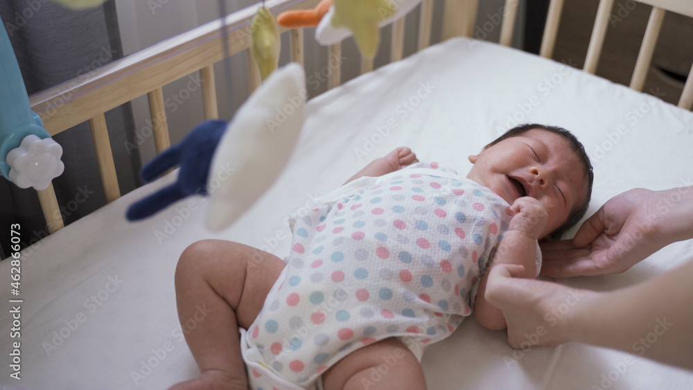 asian mother is picking up her wailing baby from the crib and ...