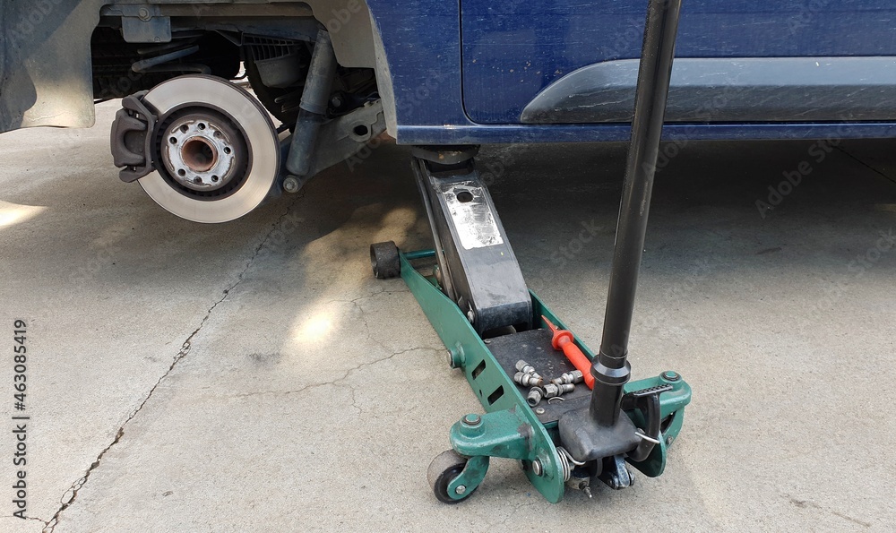 A jack lifts up a car during tire replacement. View of car disc brake ...