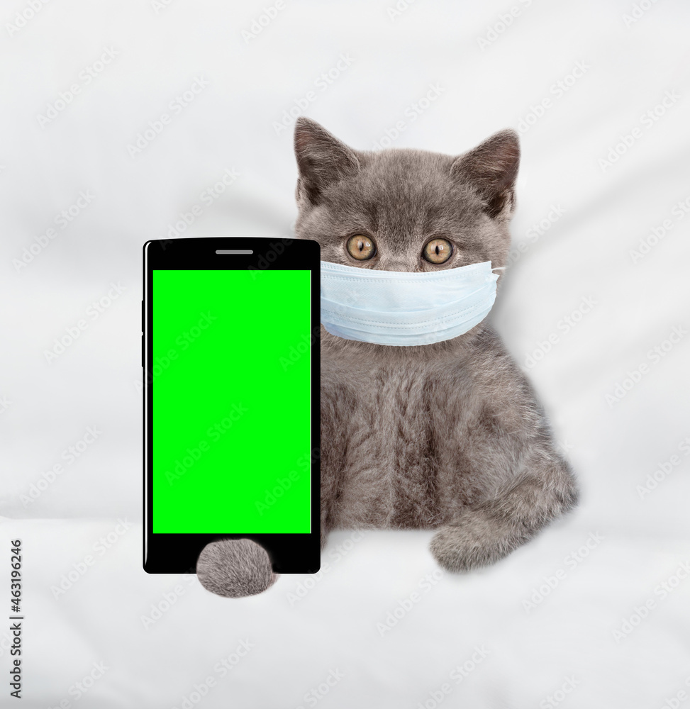 Foto de Kitten wearing medical protective mask lying under white warm ...