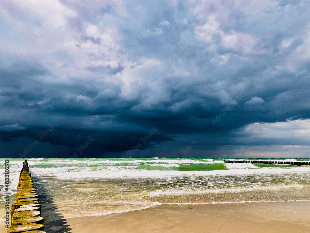 Dark huge thundercloud over a beach with light green water and Groynes ...