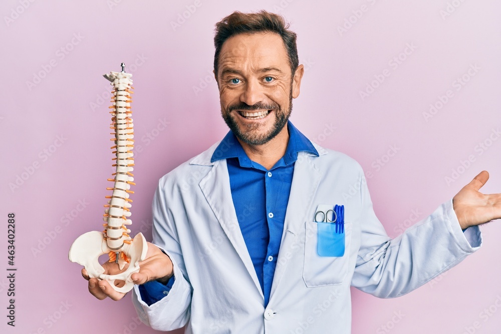 Middle age doctor man holding anatomical model of spinal column ...