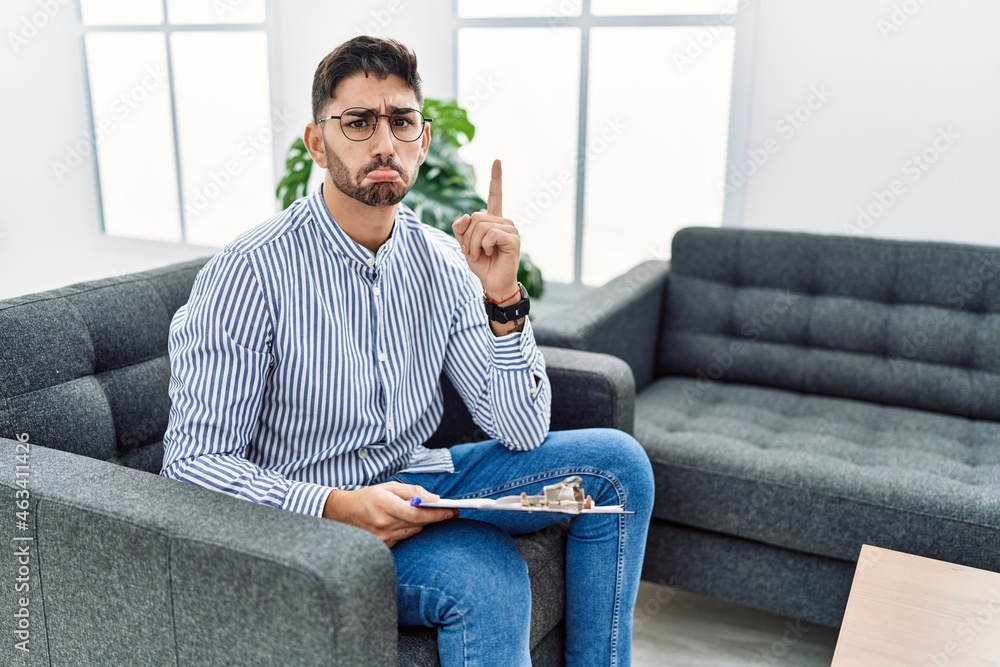 Young psychologist man at consultation office pointing up looking sad ...