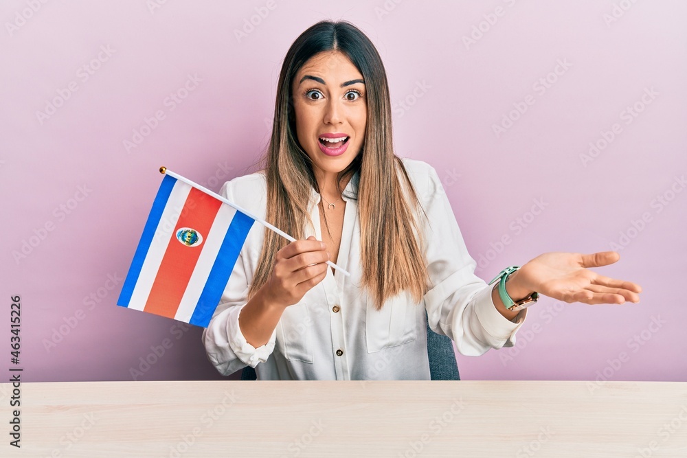 Young hispanic woman holding costa rica flag sitting on the table ...
