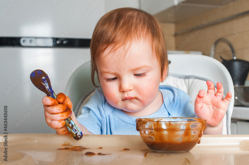Handsome red-haired baby eating in children's chair. First feeding ...