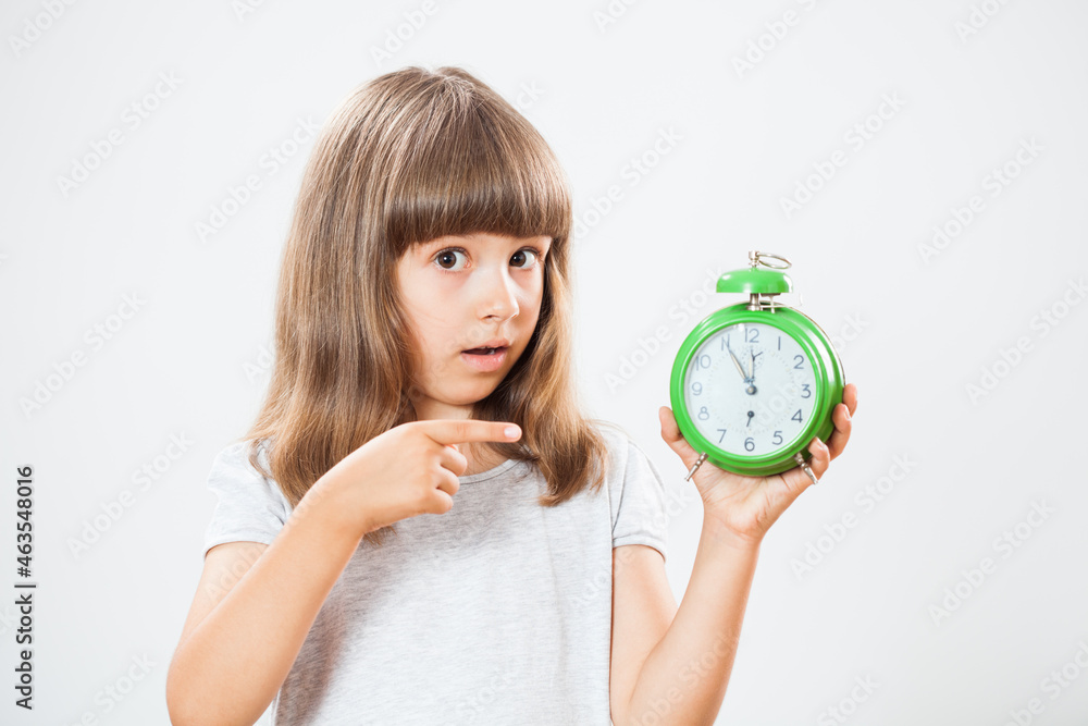 Studio shot portrait of little girl who is pointing at clock that shows ...