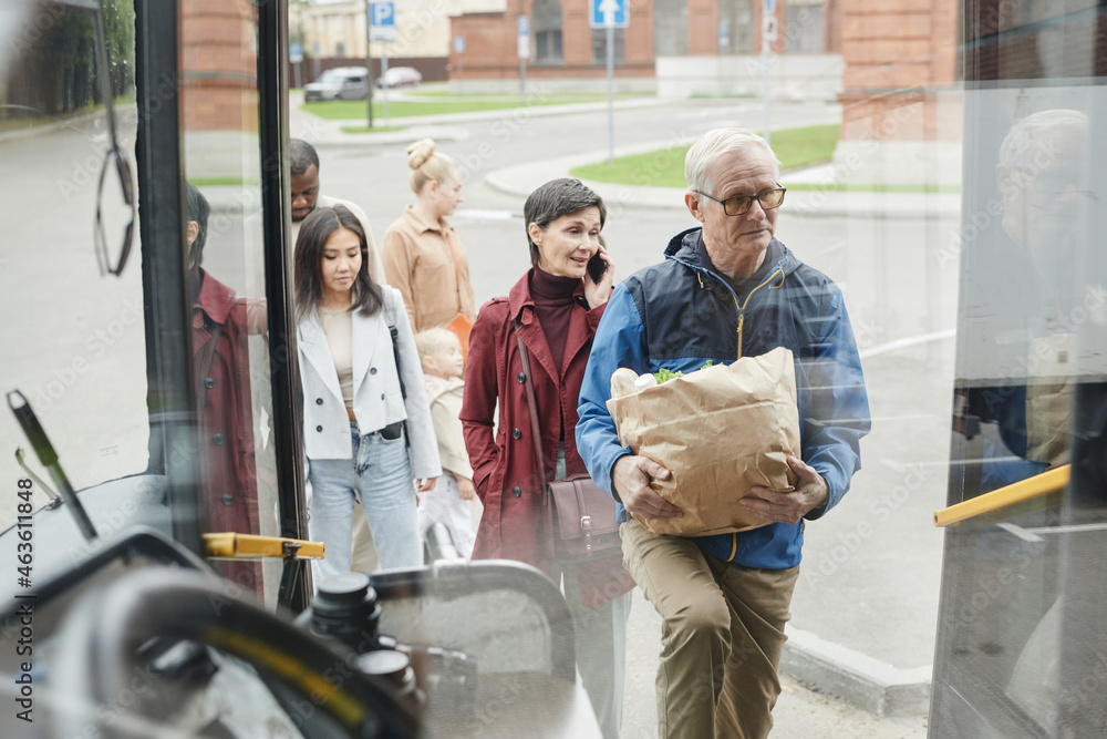 Through glass view at diverse group of people standing in line at bus ...