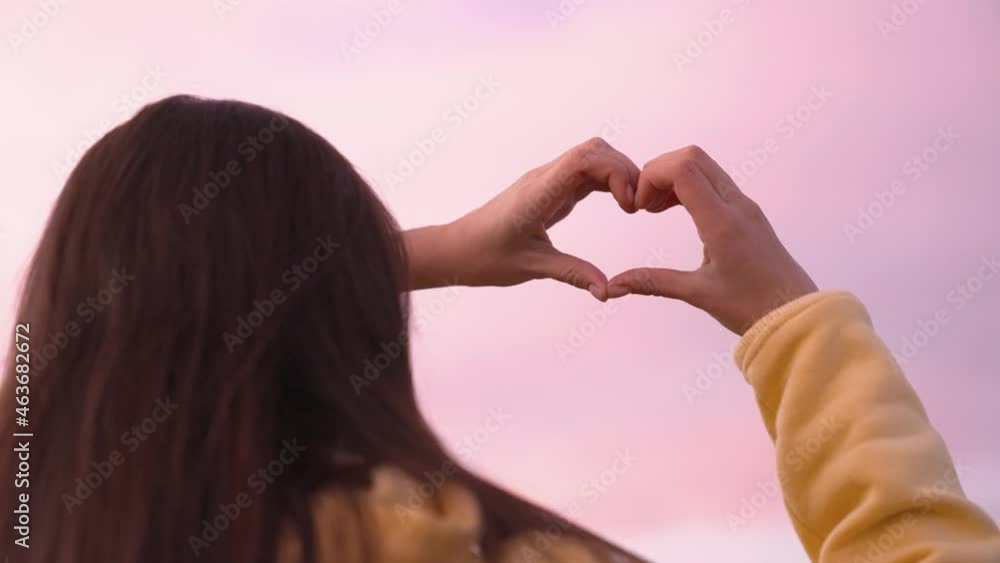 girl shows heart shape at pink sunset in the sky, romantic valentine ...