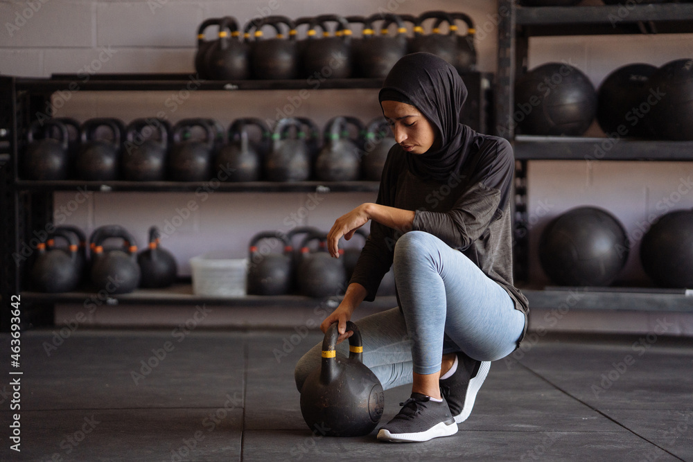 Sporty Muslim woman with kettlebell in gym Stock Photo | Adobe Stock