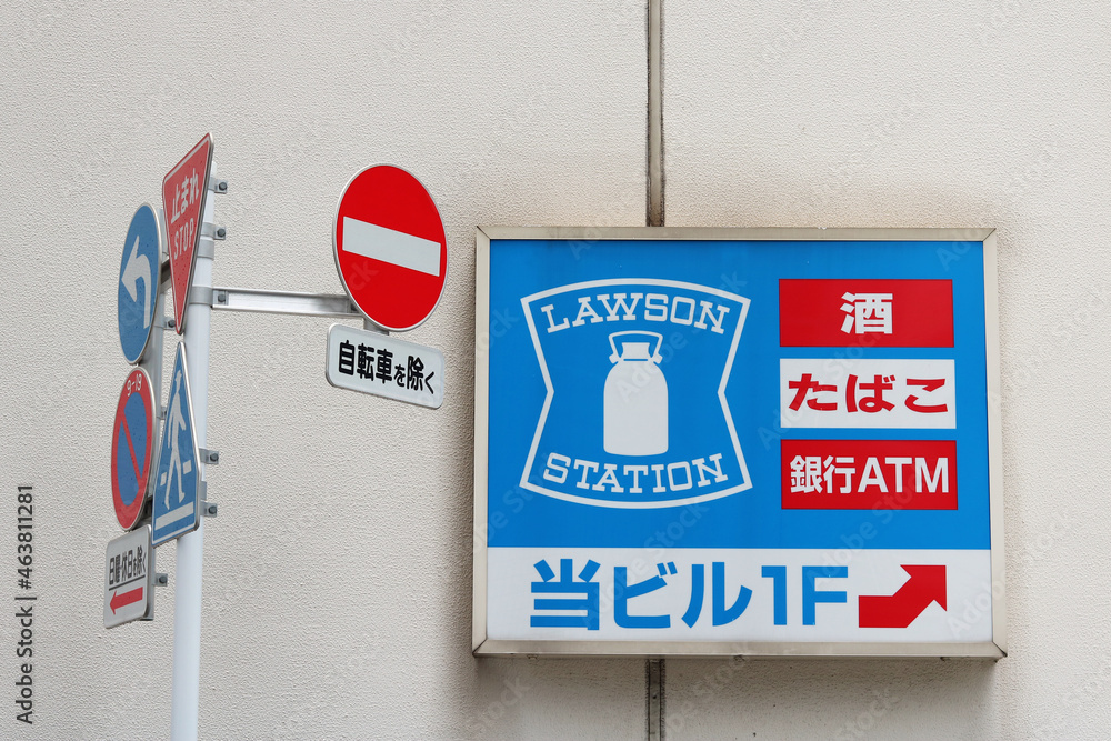 A Lawson convenience store sign on a building by some road signs in ...