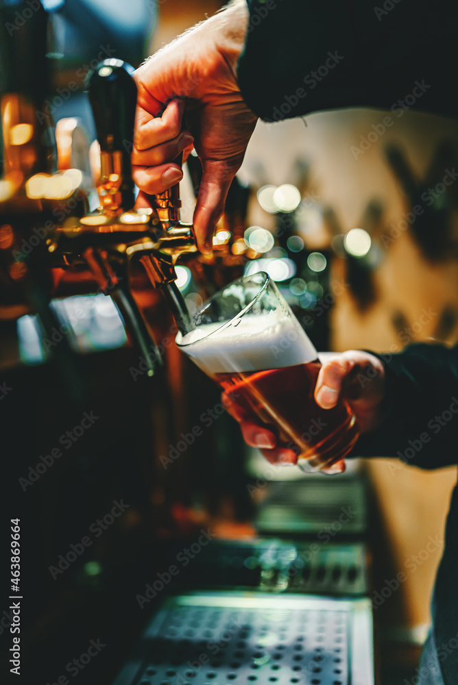 bartender hand at beer tap pouring a draught beer in glass serving in a ...