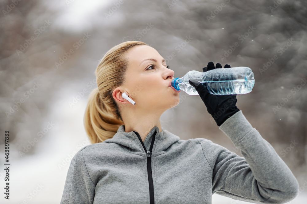 Sportswoman taking a break and drinking water while standing in nature ...