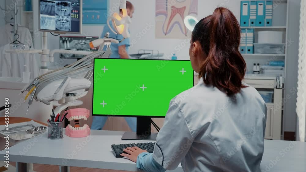 Dentist working with horizontal green screen on monitor at desk while ...