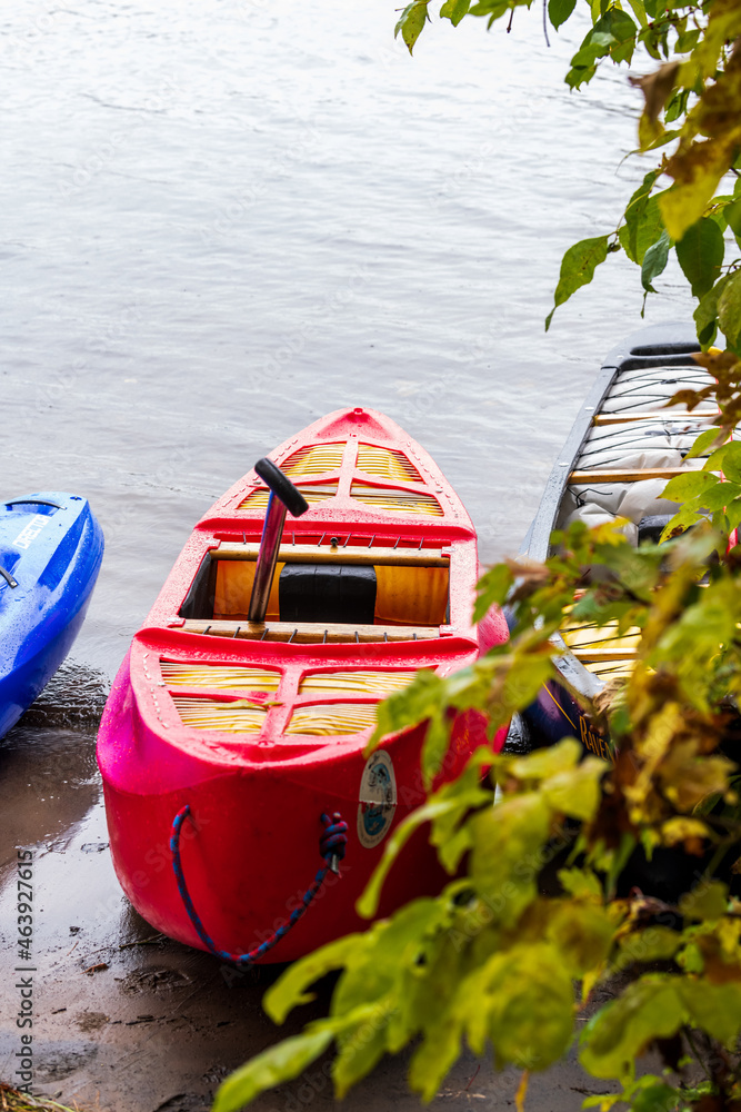 A red solo white water canoe, outfitted with air bags, sits on the bank ...
