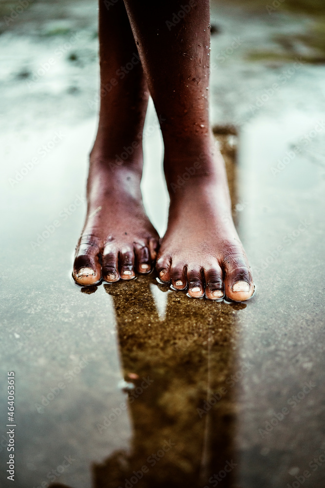 Black barefoot kid standing in puddle on street Stock Photo | Adobe Stock