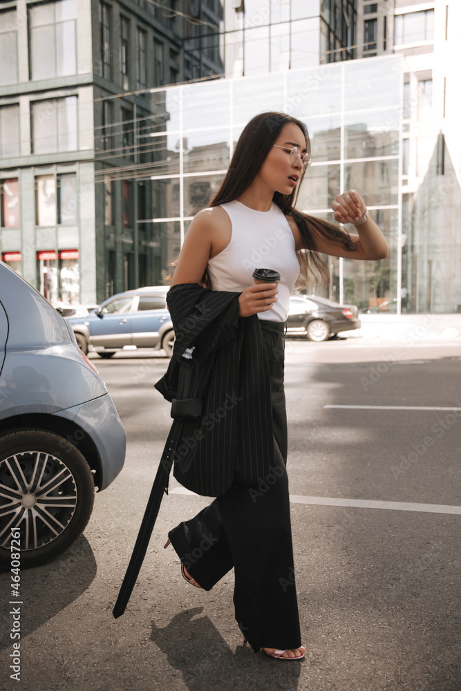 Full-length anxious young asian woman looks at watch on her hand while ...