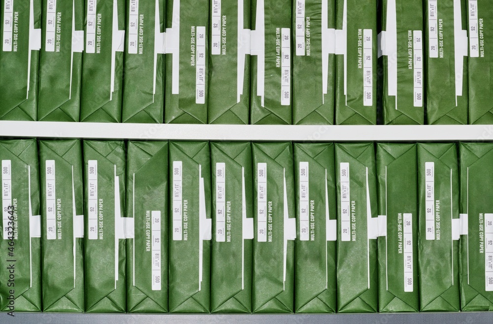 Copy paper reams with generic brand green packaging stacked up in rows ...