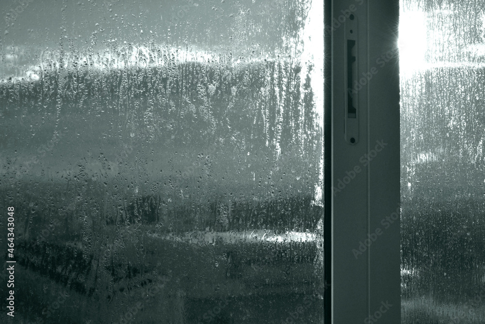 Sunlight highlights a fogged window with dripping water droplets ...