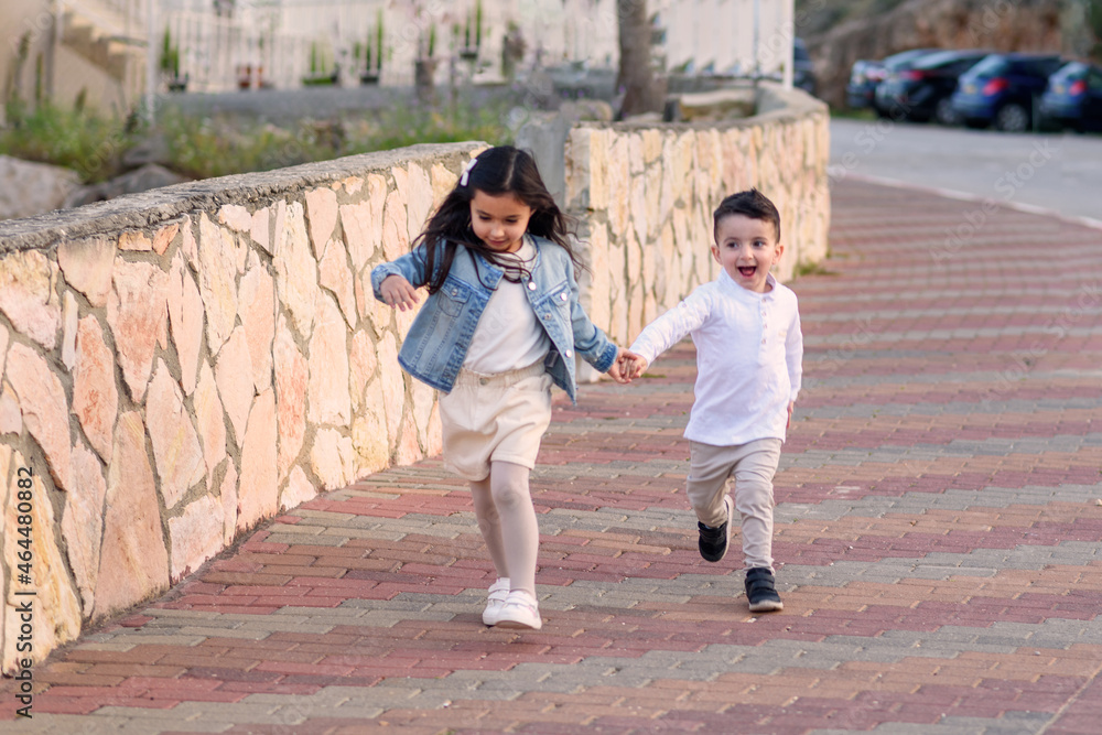 Two cute young preschool children running and playing in a city street ...