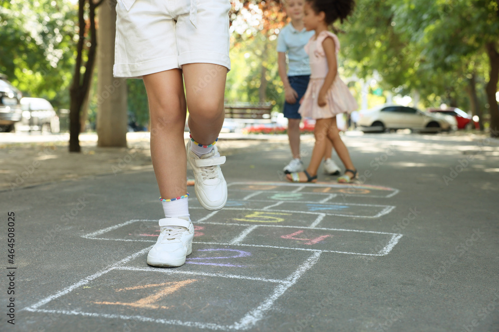 Little children playing hopscotch drawn with chalk on asphalt outdoors ...