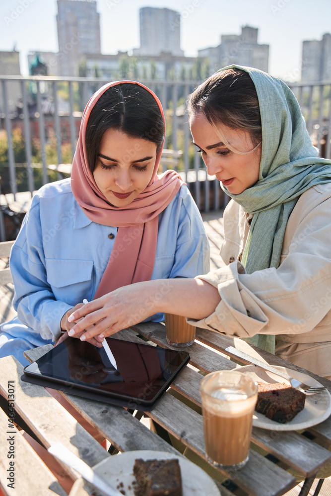 Two arabic sisters in hijab using tablet and drinking coffee together ...