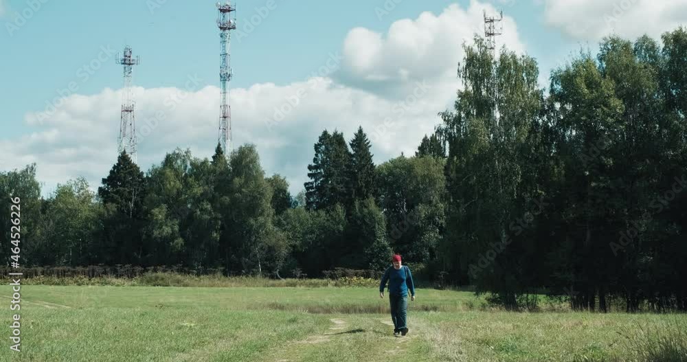 Hiker with backpack walks across field against background of 5G radio ...