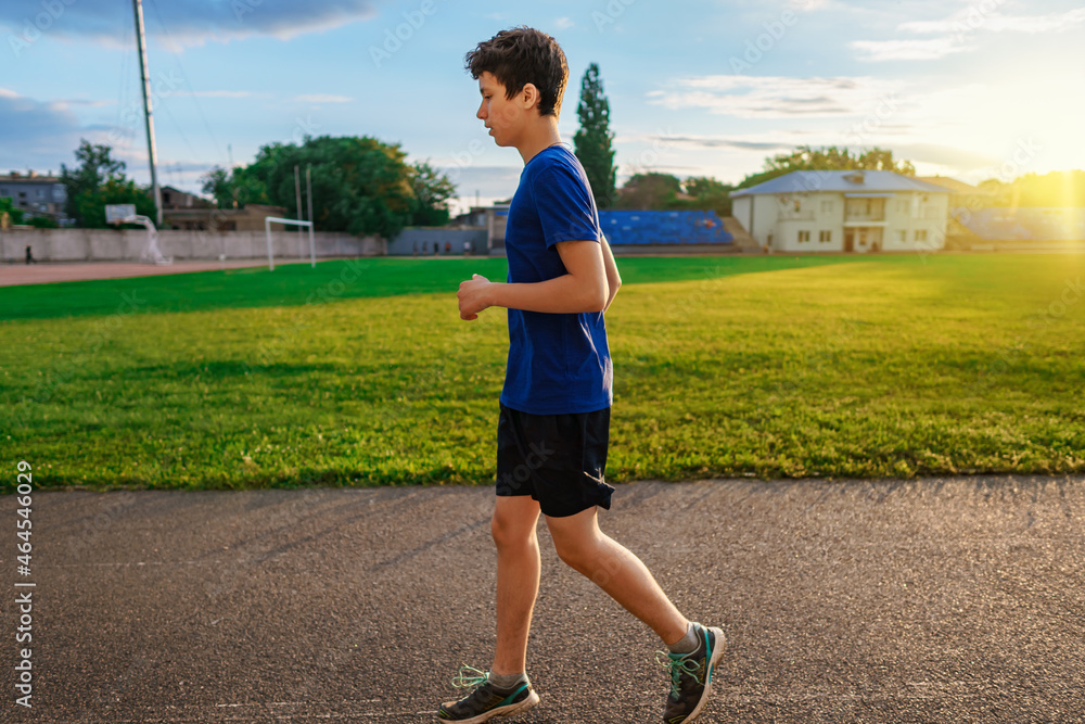 teen boy running along the stadium track, a soccer field with green ...