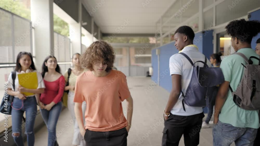 A teenage boy is standing in the high school hallways and some bullies ...