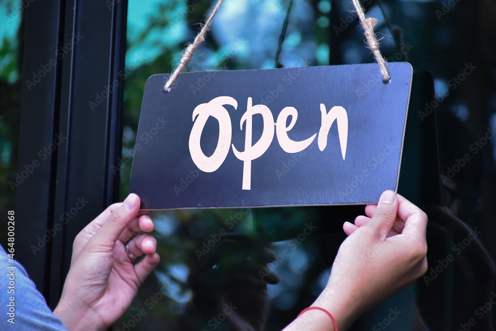 A shop owner holds label ‘Open’ which hanging on the glass door of the ...