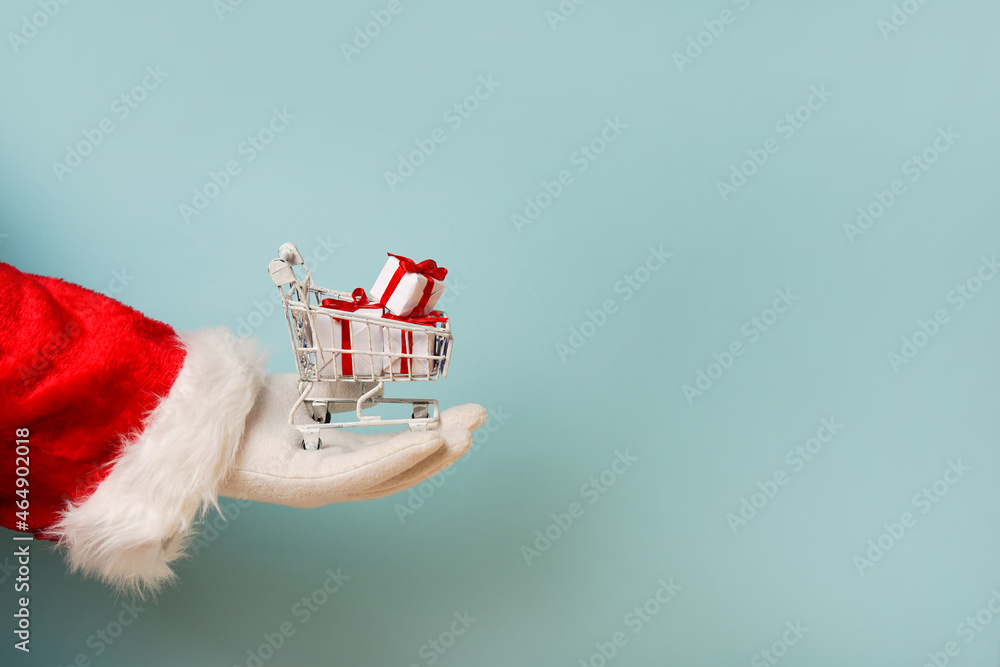 Santa claus holding a shopping cart with gift boxes on hand, blue ...