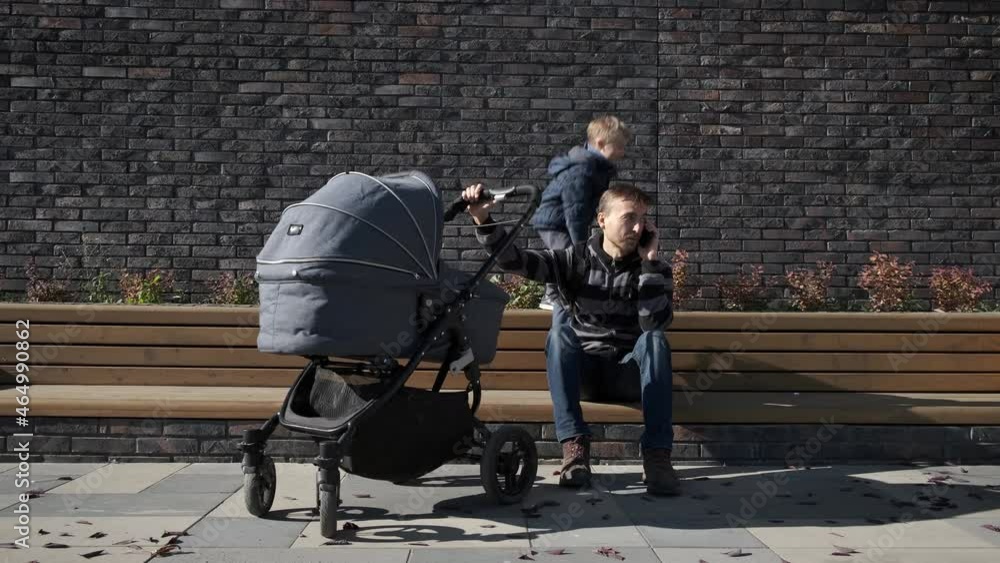 Busy father with newborn baby stroller sitting near brick wall and ...