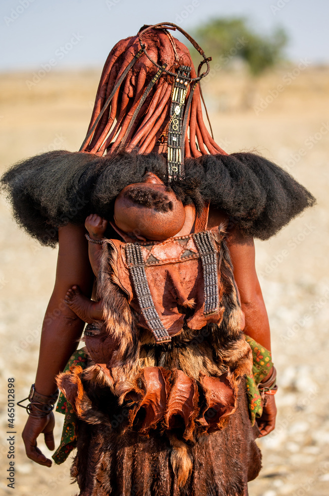 Himba tribe woman with a child behind her back in traditional dress ...