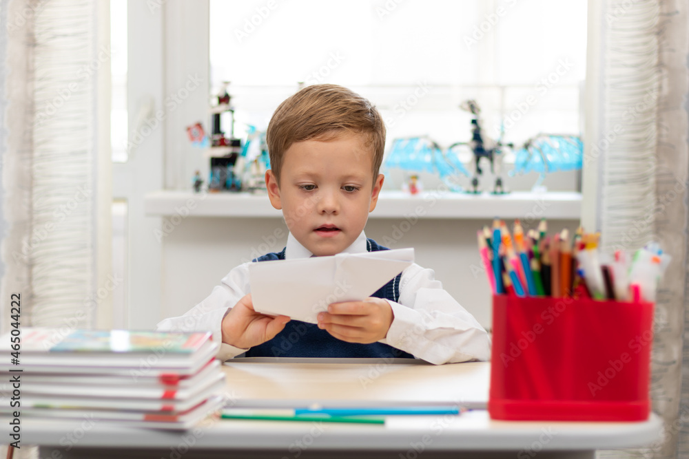 A cute first-grader boy in a school uniform at home while isolated at ...