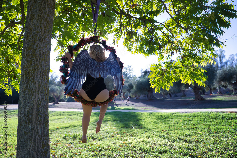 Young blonde woman in a black dress with angel wings sitting backwards ...