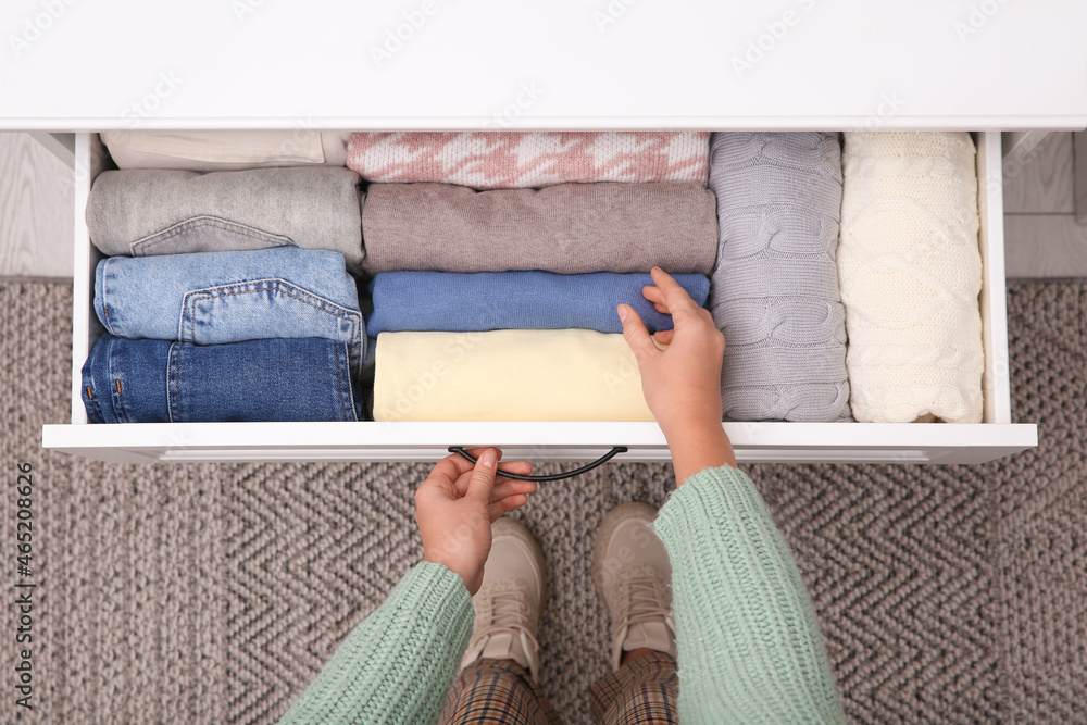 Woman opening drawer with folded clothes indoors, top view. Vertical ...