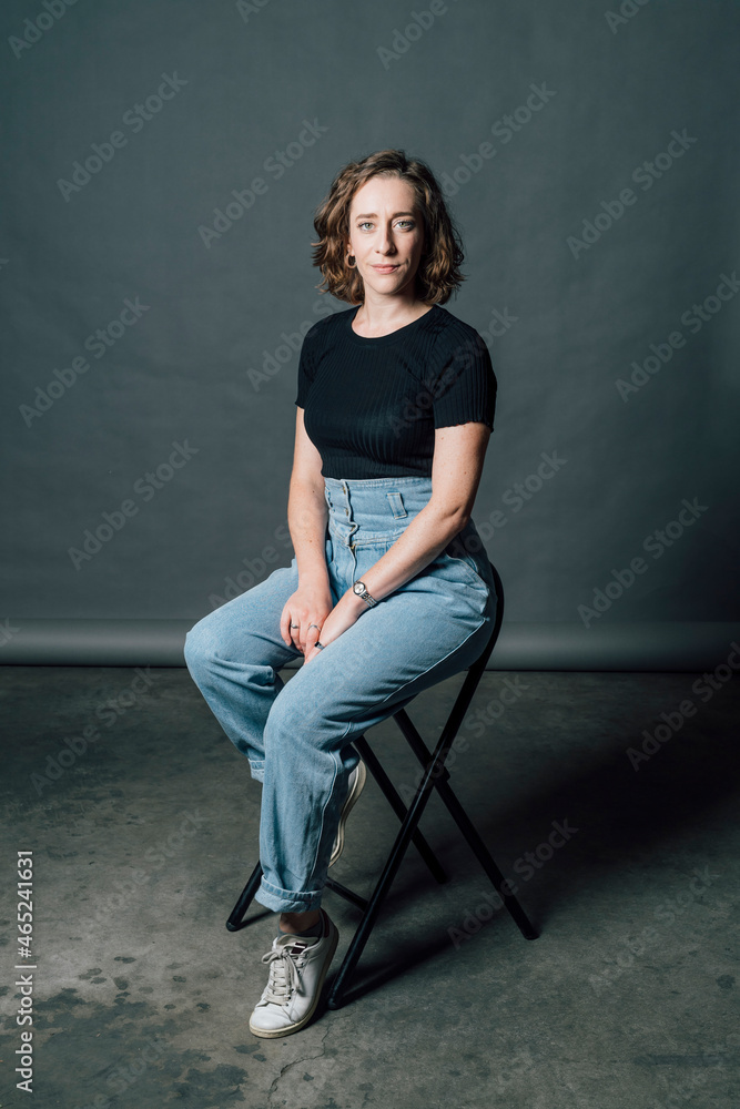 Confident woman sitting on chair in front of gray backdrop Stock Photo ...