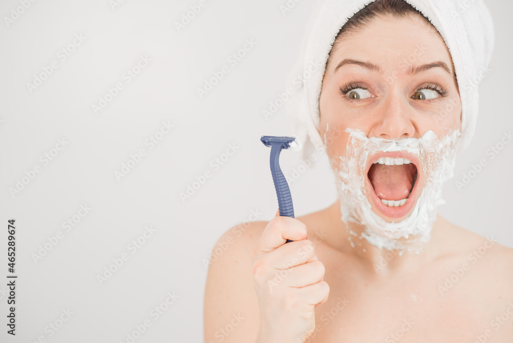 Funny portrait of a woman with shaving foam on her face holding a razor ...