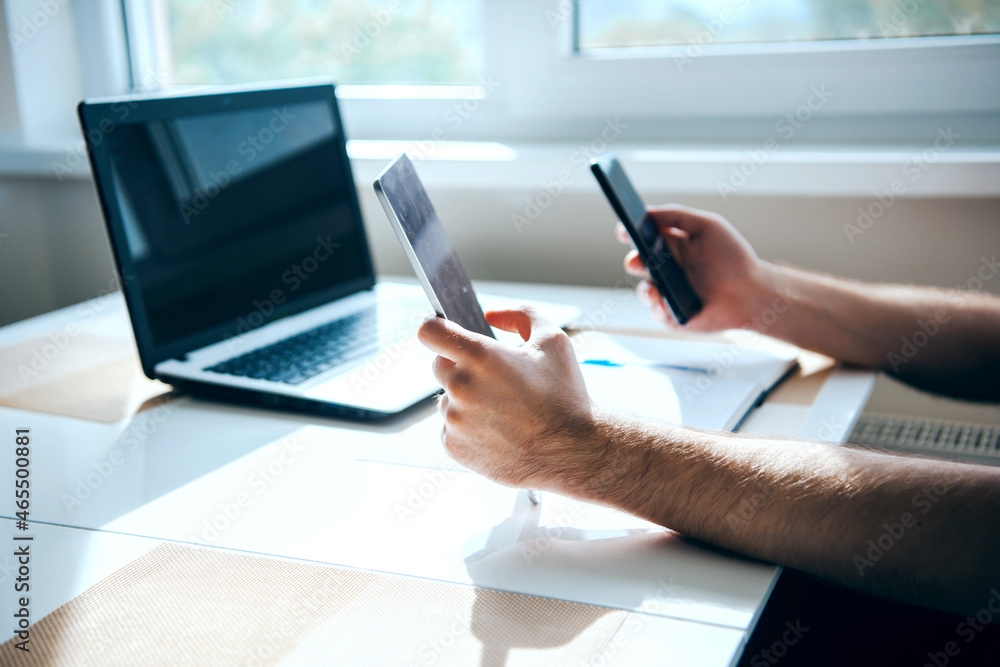 Man's hands holding two phones and a laptop on the table. Modern ...