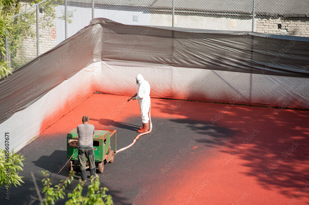 Liquid rubber coating process. A worker dressing security suit spraying ...