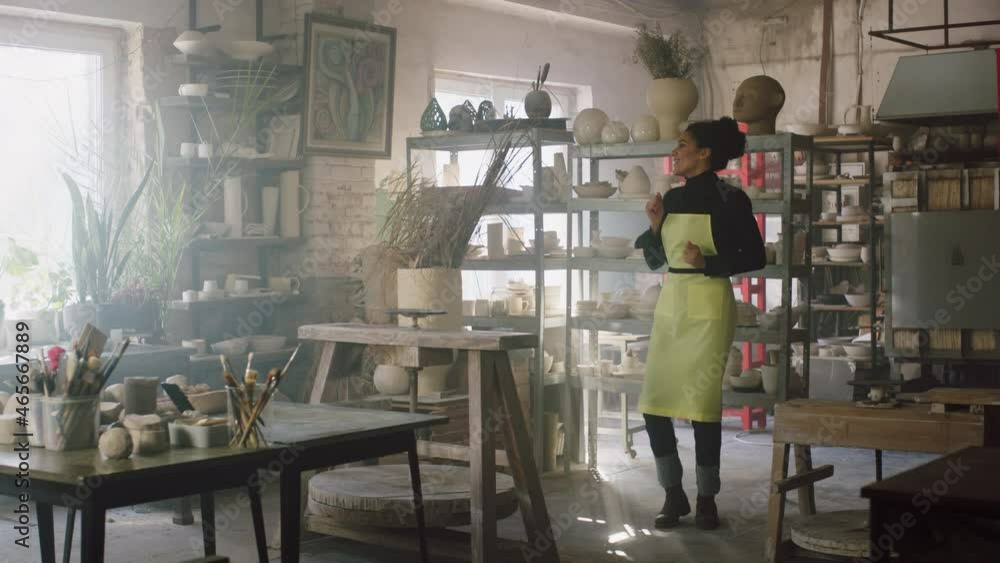 Young woman in yellow apron is dancing alone in big beautiful pottery ...