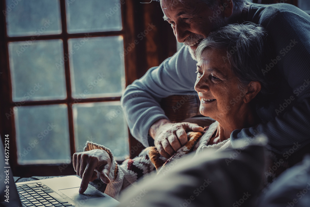 Old senior couple use laptop computer at home by night together smiling ...